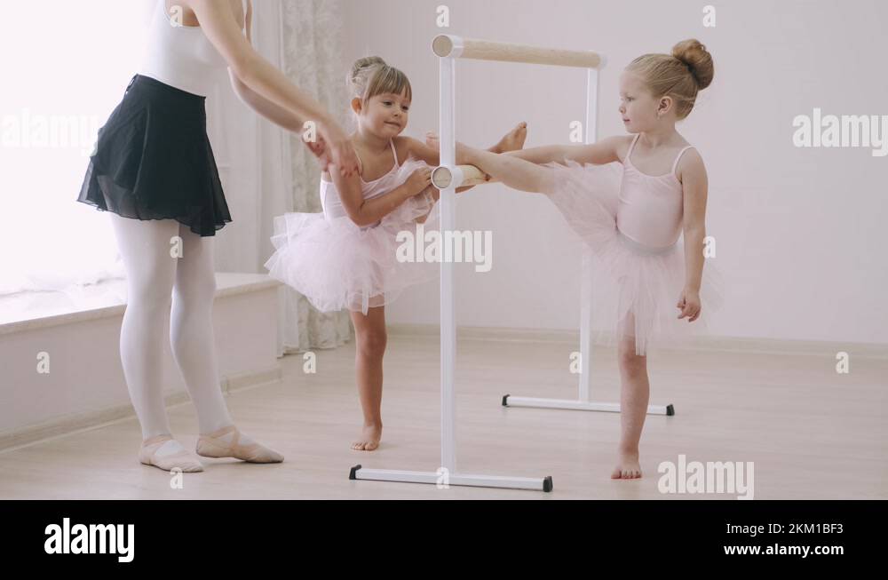Two little girls practicing choreographic elements on ballet barre with ...