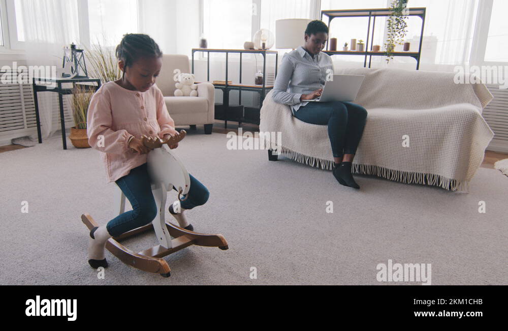Little Afro girl daughter child rides toy horse swinging playing game ...