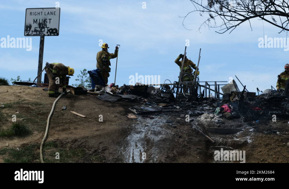 Fireman putting out a fire in a homeless encampment beside freeway ...