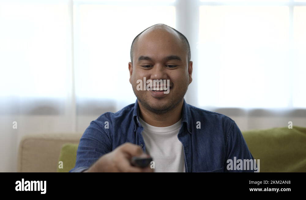 Young asian man watching television using remote to change the program ...