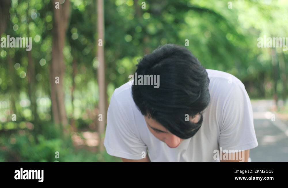 Sportive young Asian man finishing running and bending over to catch ...