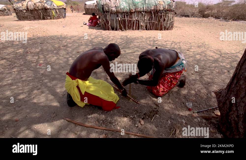 Two men of Maasai tribe light fire with traditional method. Handheld ...