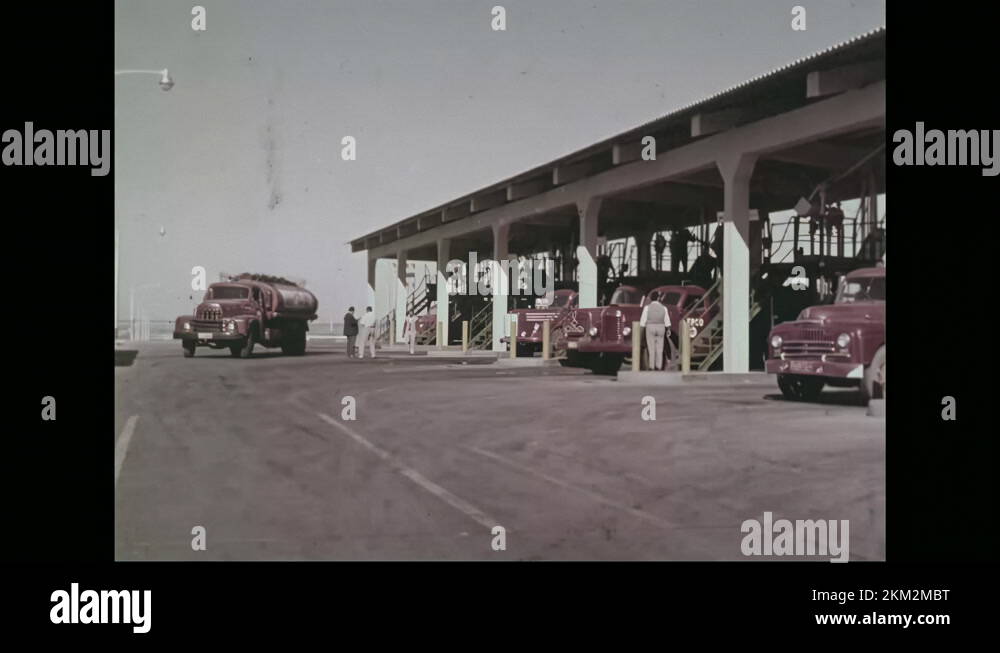 1960s: Trucks by oil refinery, truck driving. Truck drives past garage ...