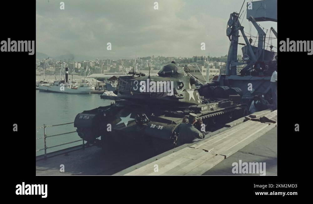 1960s: Armored vehicle on dock. Ships in harbor. Tank lowered onto deck ...