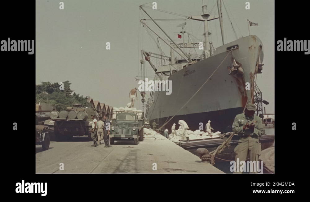 1960s: Tank navigates dock as men unload ship. Tank lowered onto deck ...
