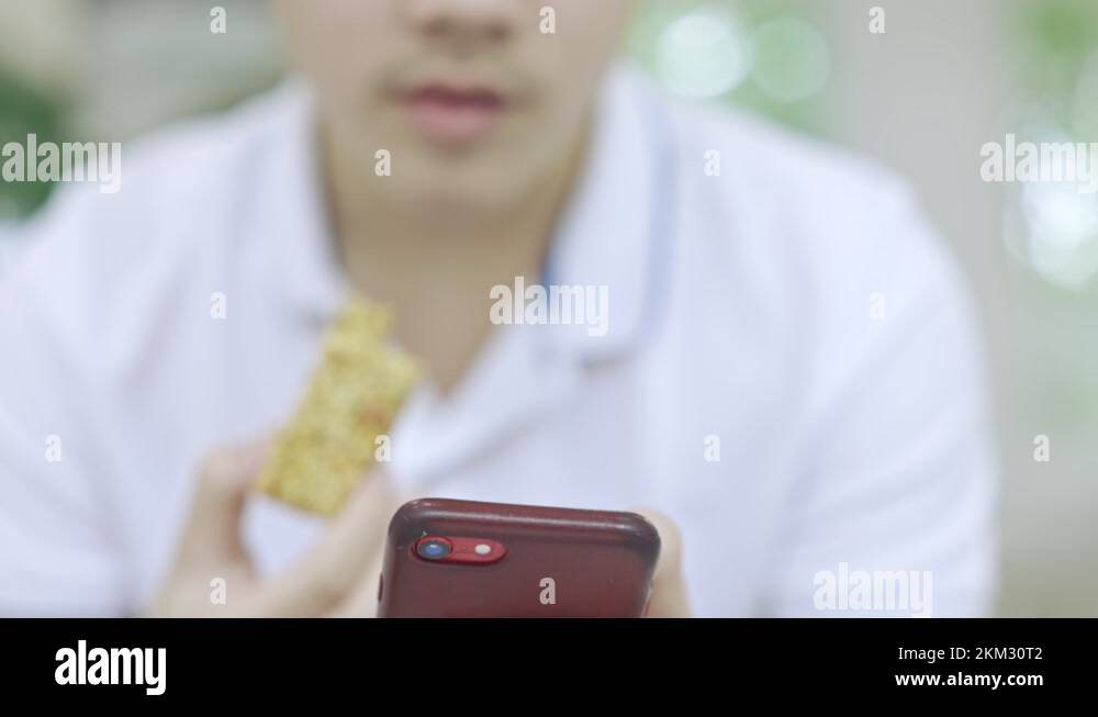 Asian teen boy eating snacks While using the phone at the same time ...