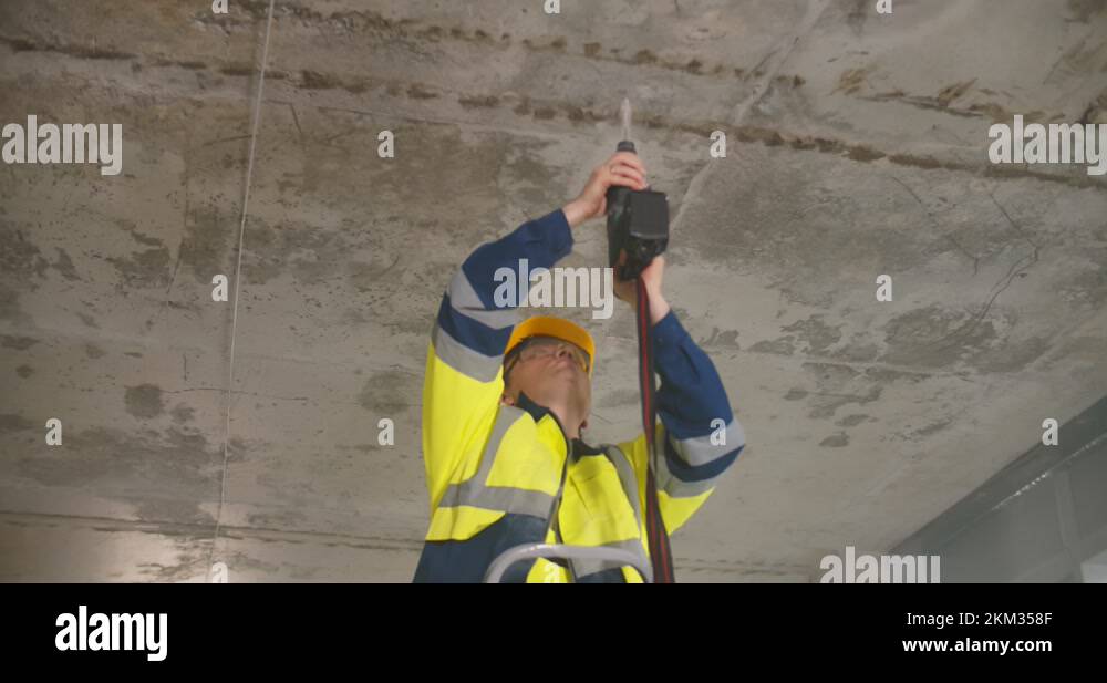 Construction worker drilling hole on ceiling with electrical drilling ...