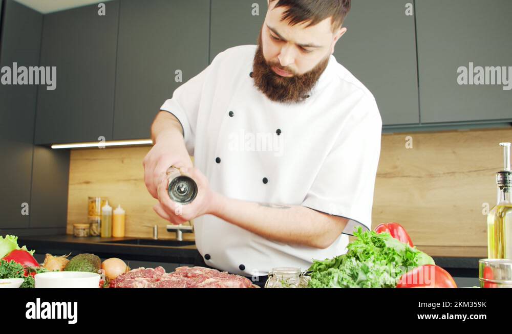 Young chef salting food in a modern kitchen. The man prepares food at ...