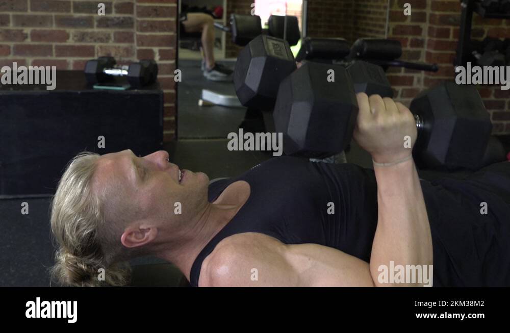 Muscly man in home gym exercising close grip dumbbell bench tricep ...