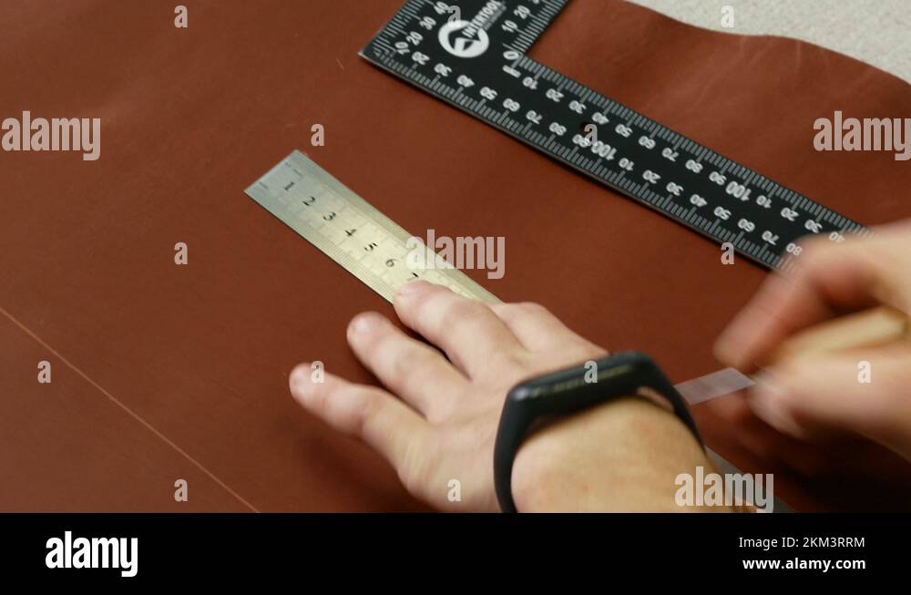 Craftsman makes a line of markings on the leather cloth using a ruler ...