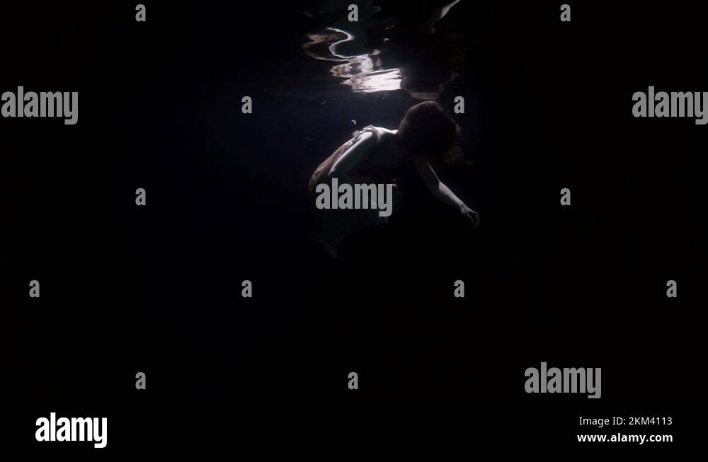 corpse of sunken woman is floating in dark depth, underwater shot of ...
