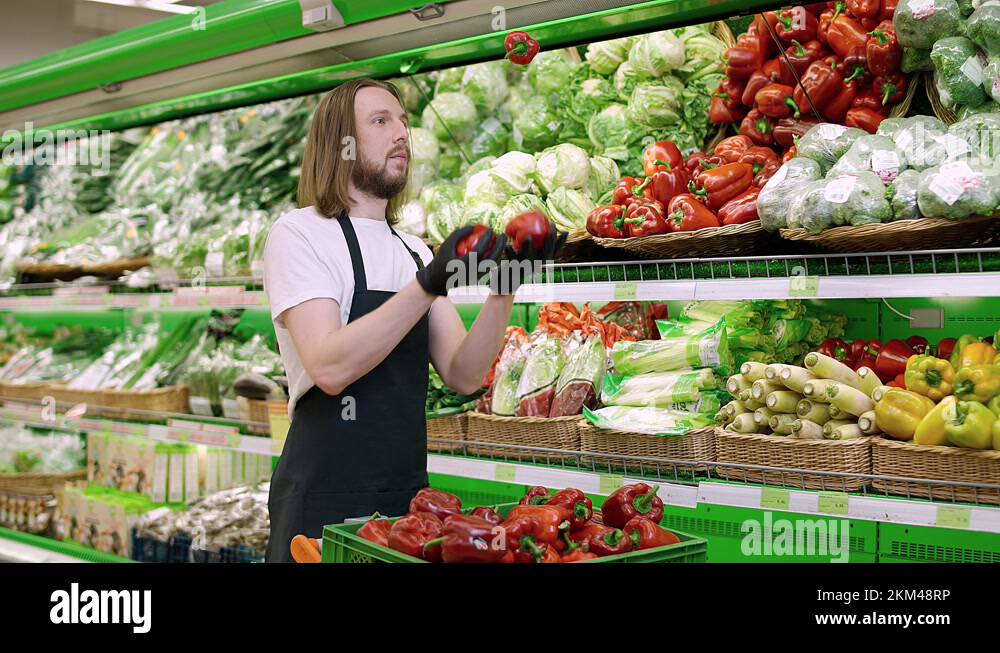 Man replenishes products on the shelves, juggles red pepper fruits ...