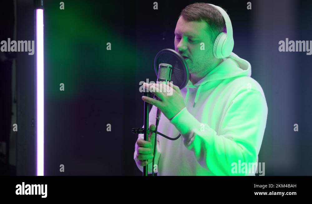 Attractive unshaven artist puts on headphones and sings into microphone ...