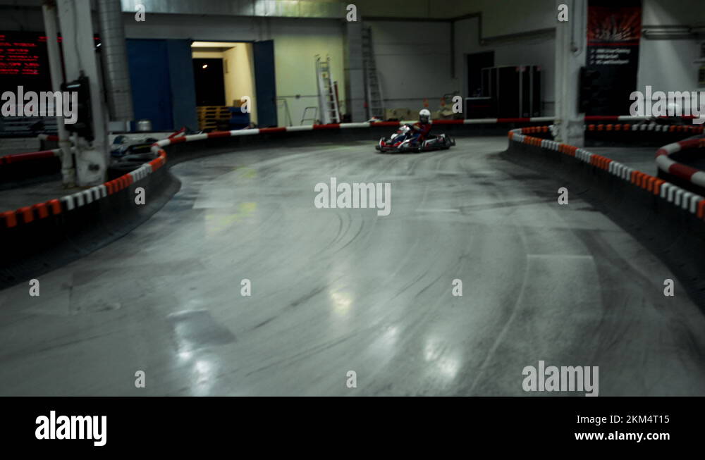 Two kart driver wearing helmets and racing suits drive over an indoor ...