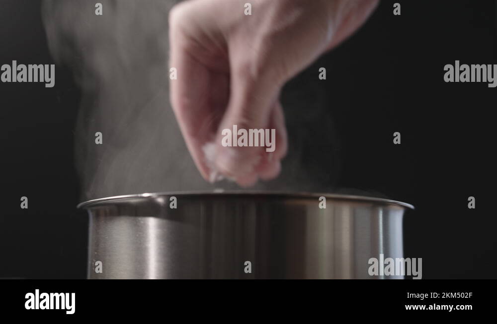 Man hand adding salt to boiling water in pot over black background ...