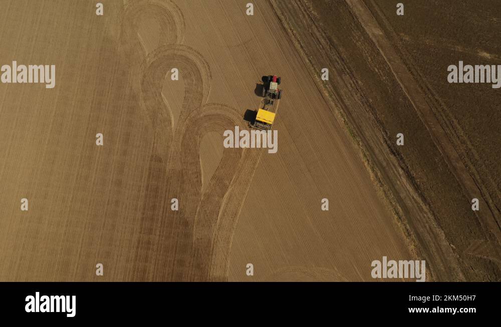 Tracking aerial view of a red double wheeled tractor with yellow seeder ...