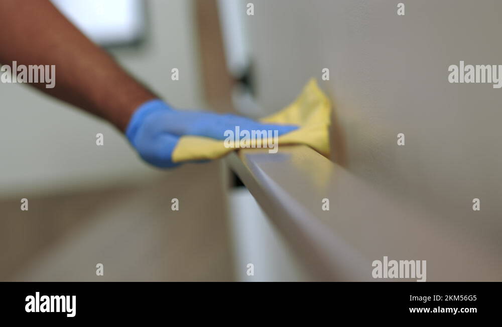 A young man cleans the stair handrail by spraying a cleaner to kill ...