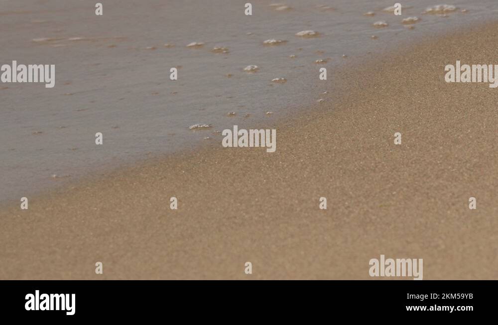 Close-up Sea waves roll over the sandy shore. Water seeps into the sand ...