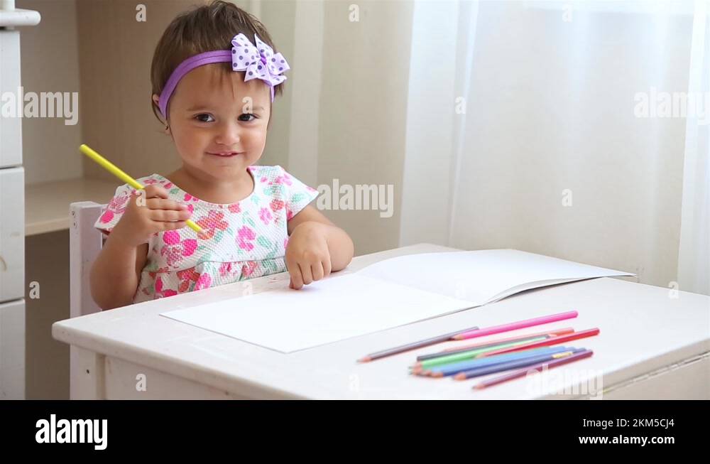 Little girl learning to draw on a piece of paper with colored pencils ...