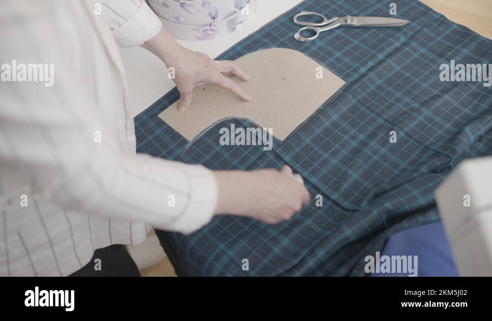 Tailor using sewing pattern, marking fabric, making dress in workshop ...