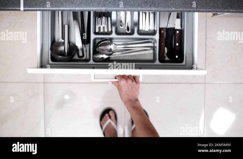 Girl in the kitchen pulls out a drawer with a set of chrome cutlery ...
