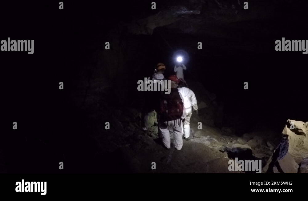 Four spelunkers in white suits explore a dark chamber in deep cave ...