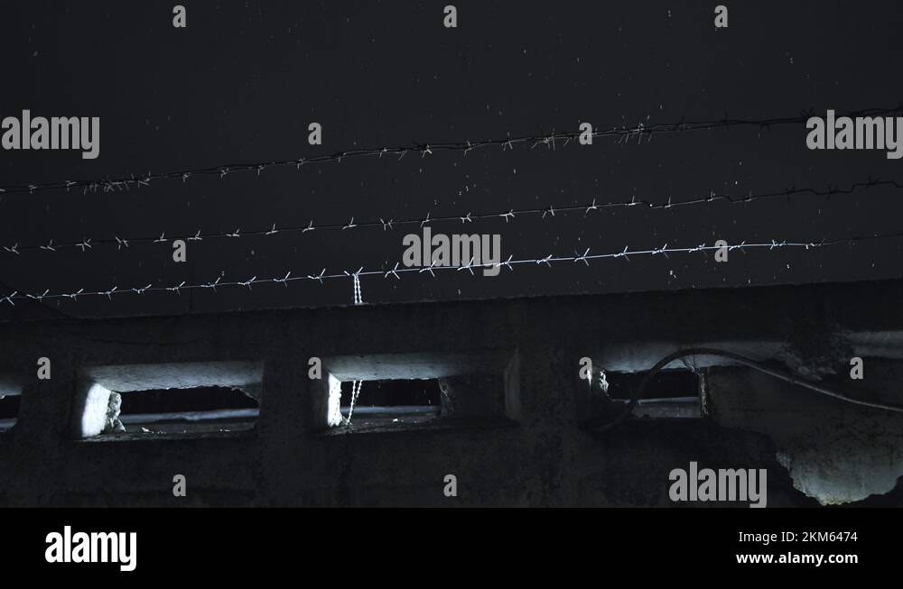 prison barbed wire over concrete fence at cold dark winter night during ...