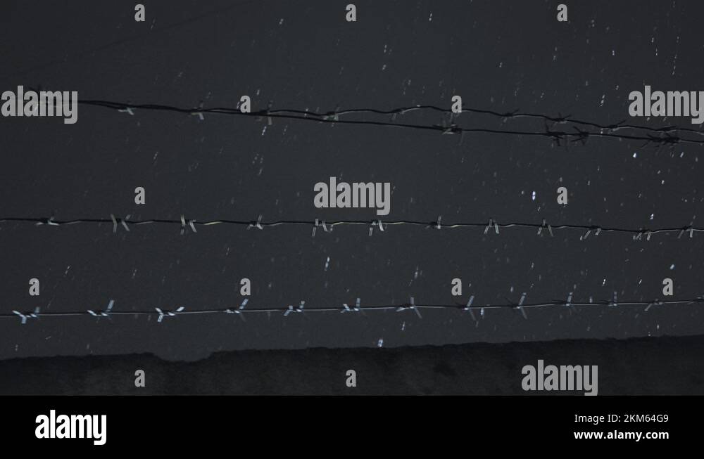 prison barbed wire over concrete fence at cold dark winter night during ...