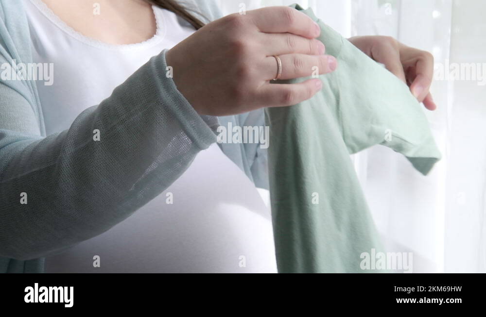 4k Pregnant mother holding baby clothes in hands. Happy Expectant ...