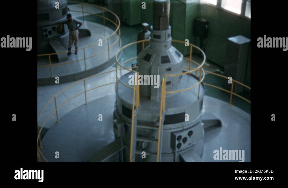 1960s: Three generators inside hydroelectric dam. Two men in station ...