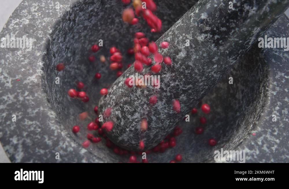 Close-up of spicy rose peppercorns falling and bouncing in a grey stone ...