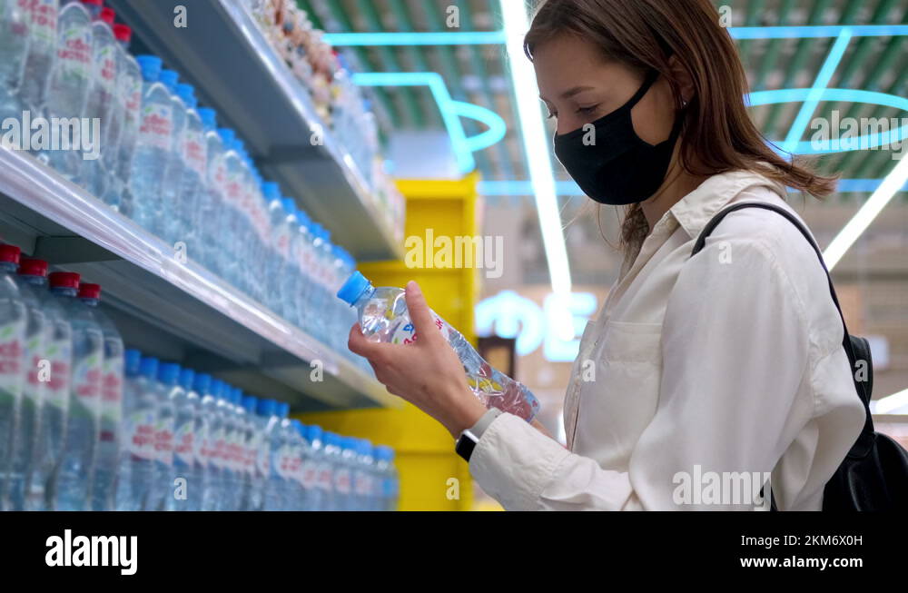 buying drink water in supermarket, female customer is reading label on ...