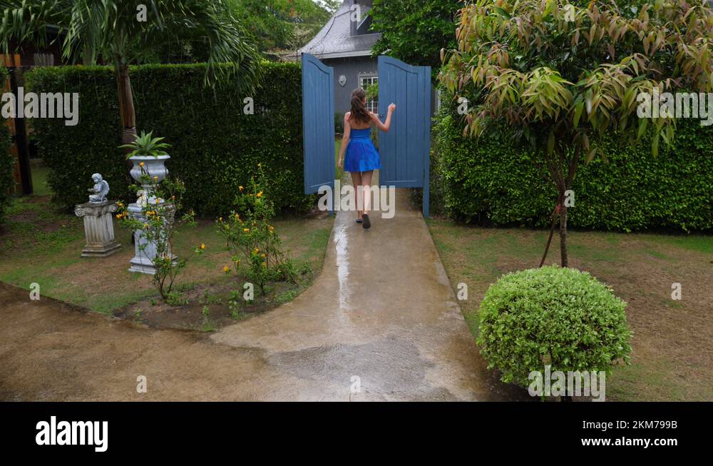 Cheerful woman run to small gate, pass through and glance back, rainy ...