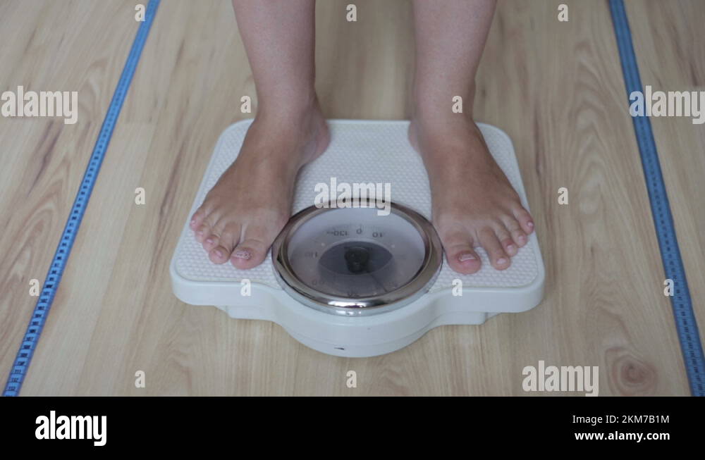 Young woman checking her weight. Close-up of female legs on the scales ...