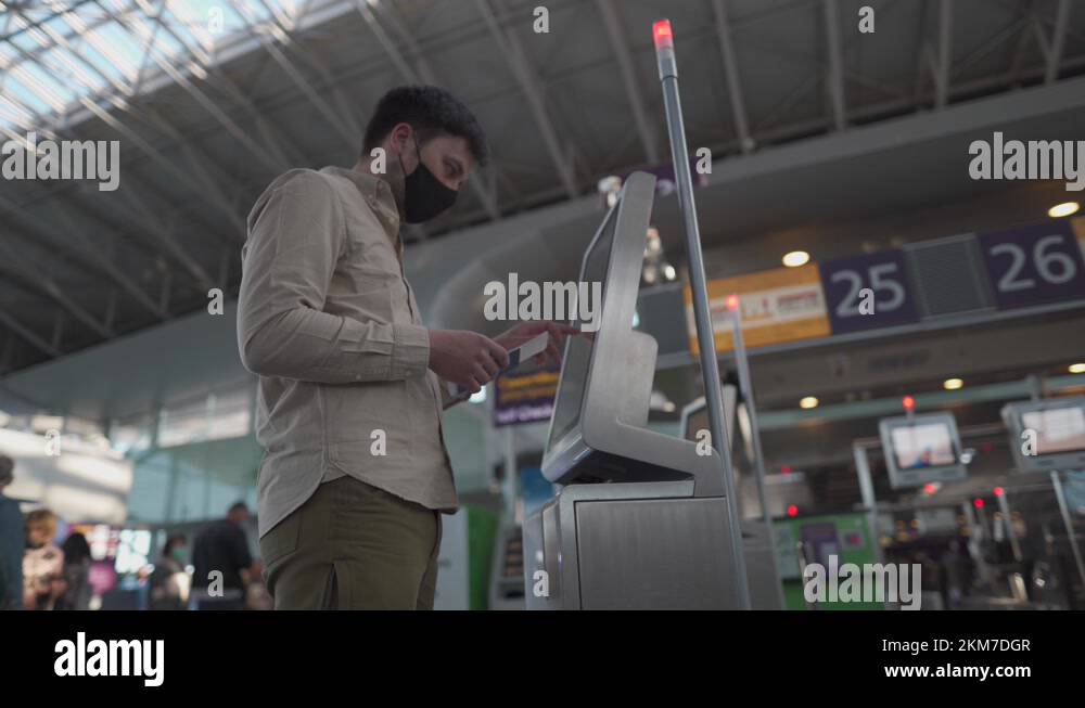 Man in protective mask using self check-in kiosk in airport. Male use ...