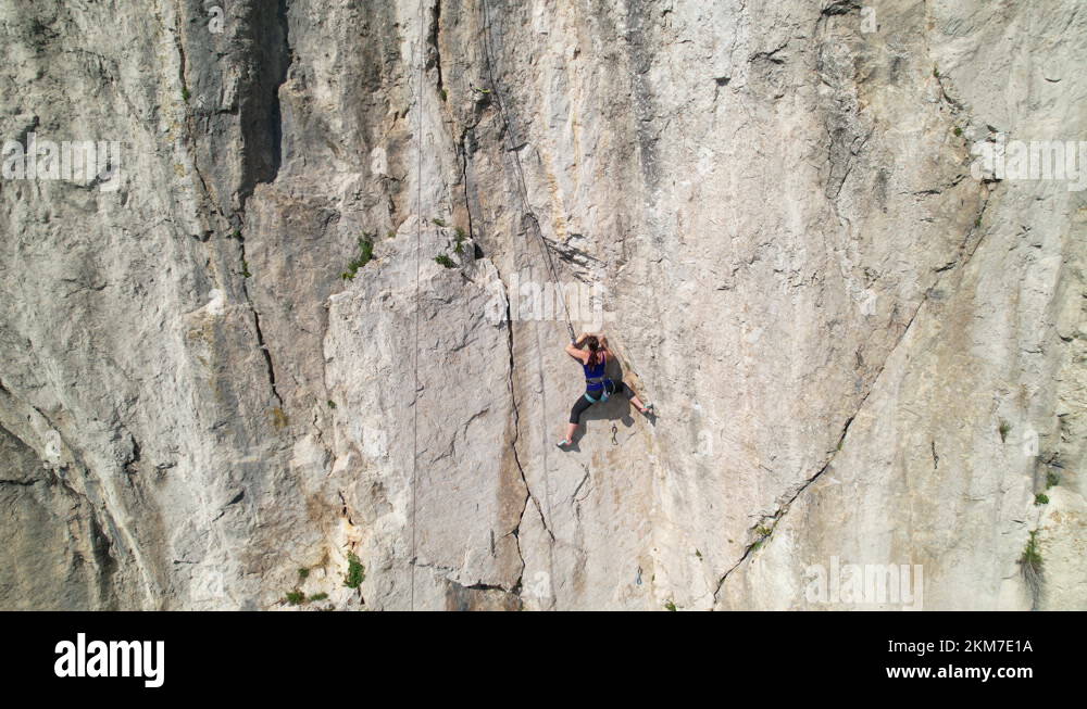 AERIAL: Flying view of the landscape surrounding woman rock climbing in ...