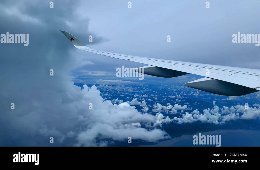 Wing of Qatar Airways Plane cruising into massive clouds with blue sky ...
