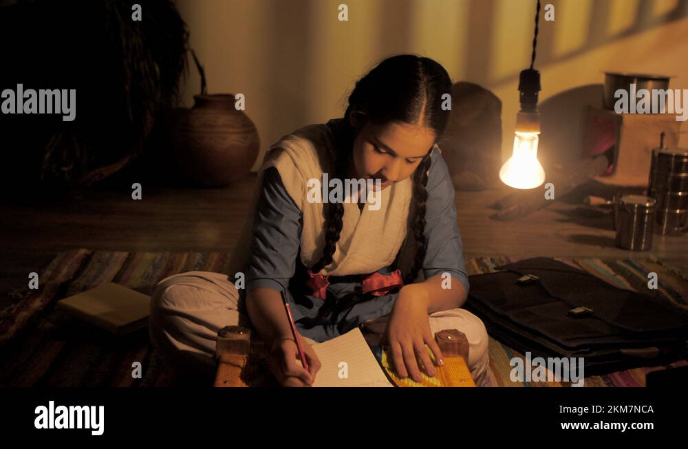 Village girl sitting on a mat taking down notes under the light in the ...