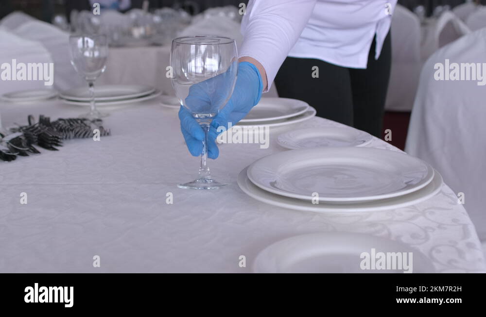 Waiter serves banquet table with blue gloves. Spoons, forks, glasses ...
