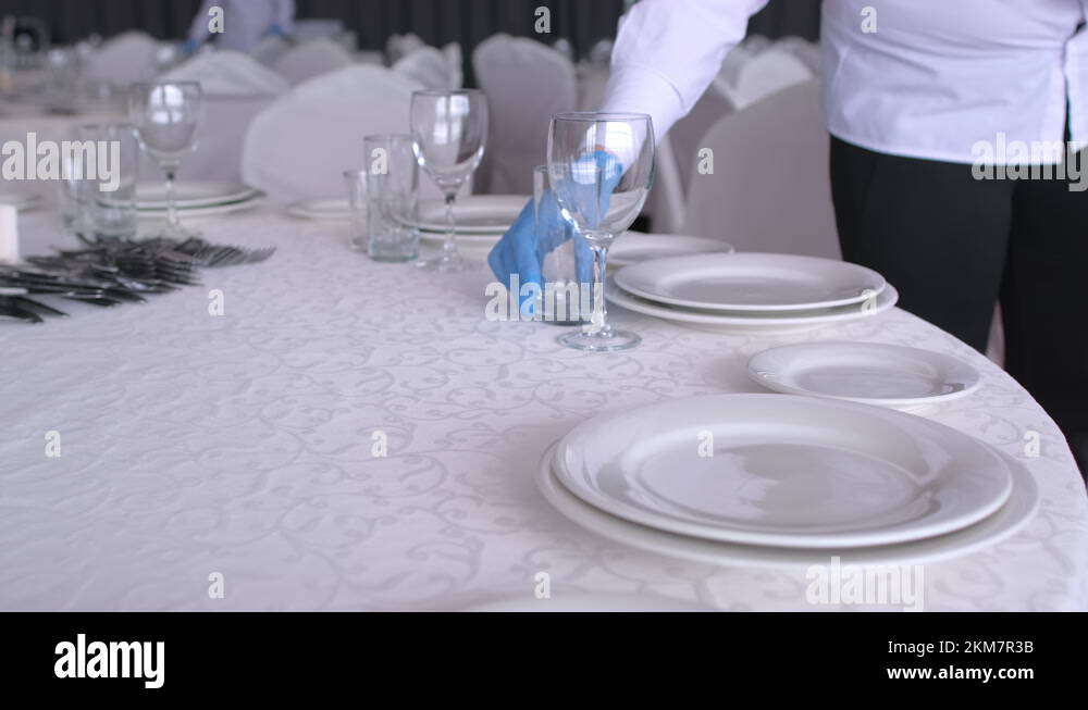 Waiter serves banquet table with blue gloves. Spoons, forks, glasses ...