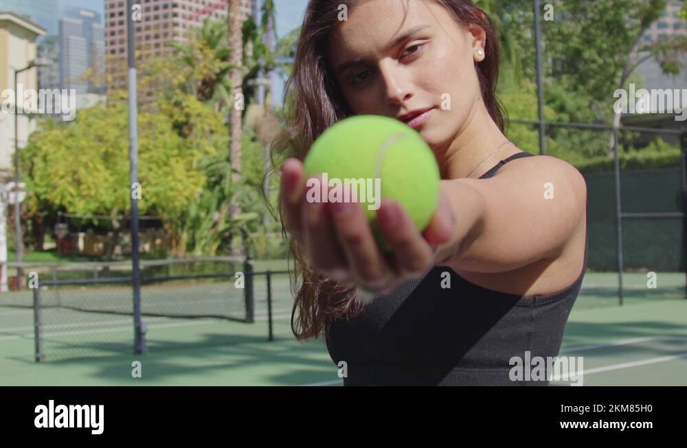 Beautiful model on the tennis court holds a tennis ball in front of the ...