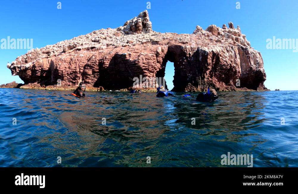 Snorkelers float in the water just offshore from an arch rock formation ...