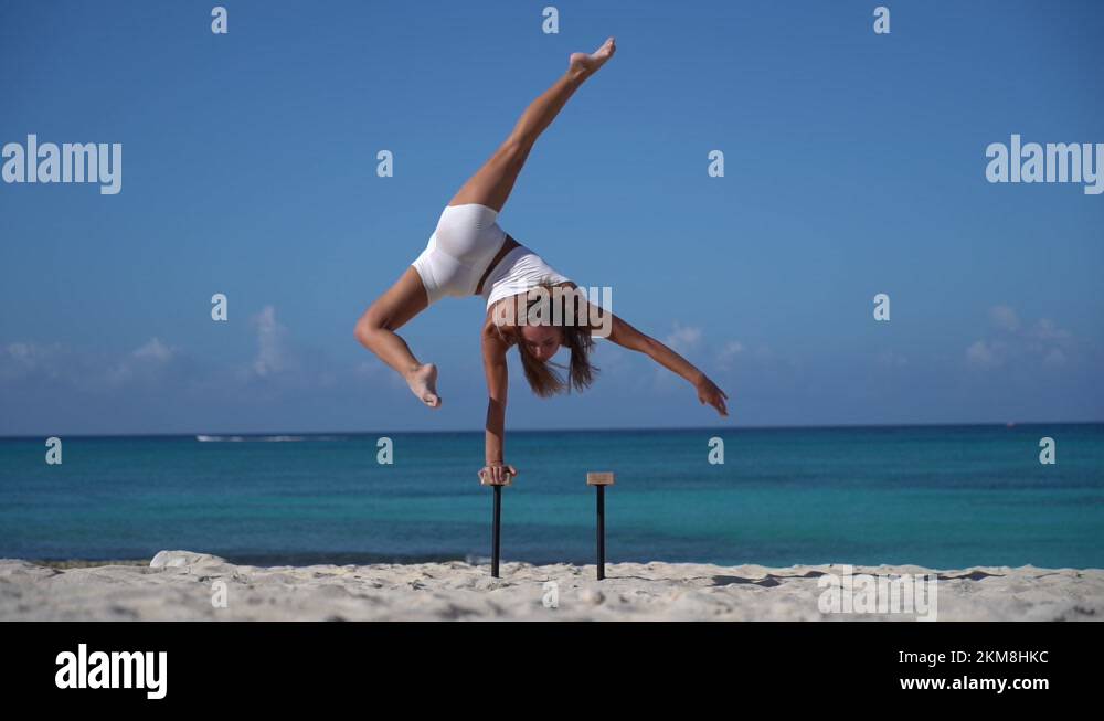 Woman wearing white doing handstand on the beach with sea. Healthy ...