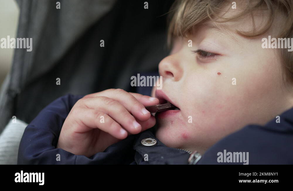 Toddler boy eating piece of chocolate. Child takes a bite of snack ...