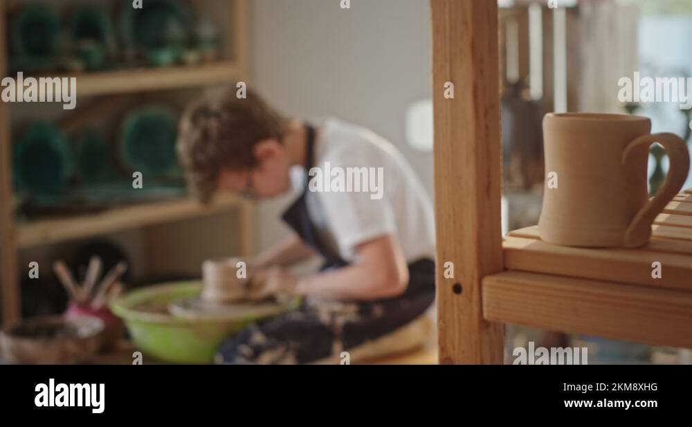 A young teen boy is engaged in pottery sitting in a potter's wheel ...