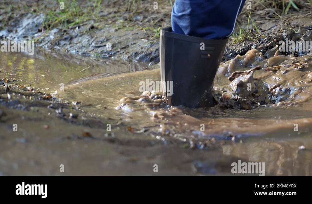 Unrecognizable man in rubber boots steps into a muddy puddle, water ...