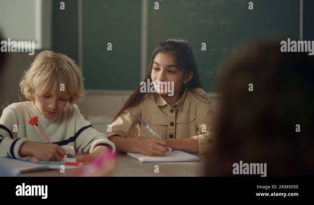 Students learning at round table in school. Pupils writing text in ...