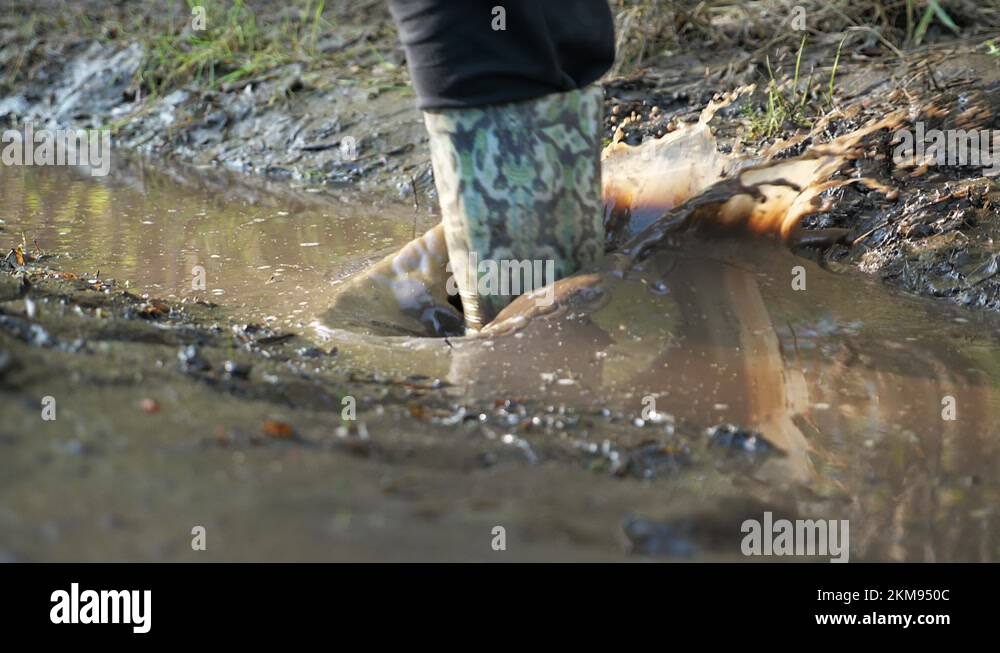 Unrecognizable woman in rubber boots steps into a muddy puddle ...