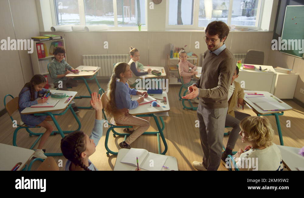 Teacher asking questions to students in class. Schoolchildren raising ...