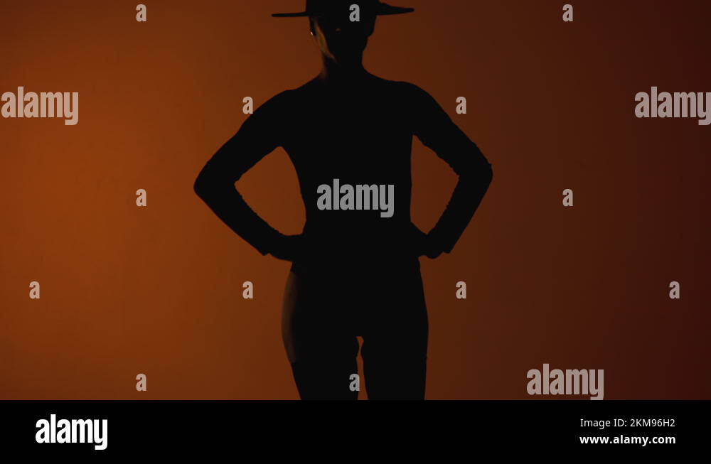 Woman in hat, bodysuit and stockings under flashing orange light ...